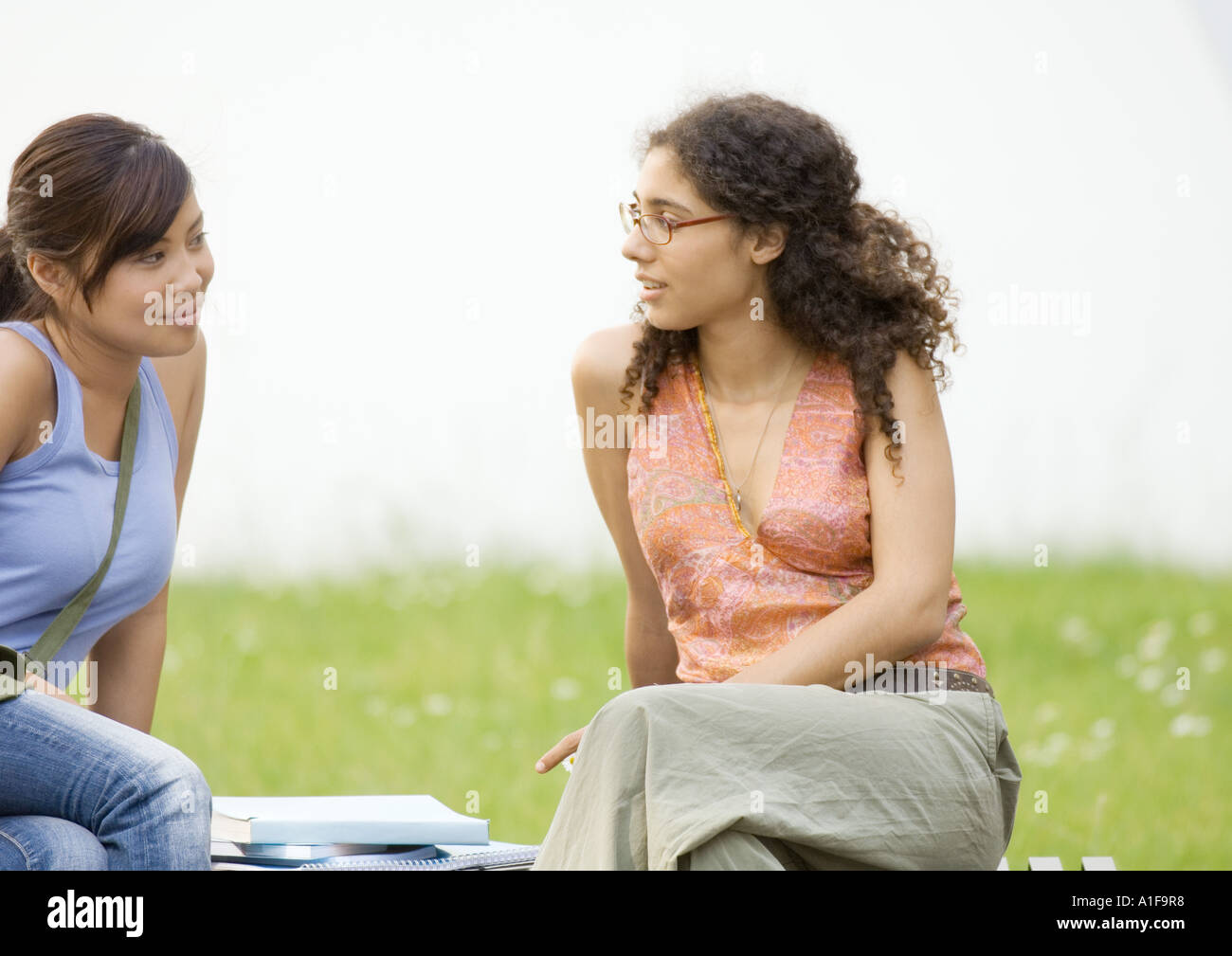 Two young women sitting on bench together, talking Stock Photo - Alamy
