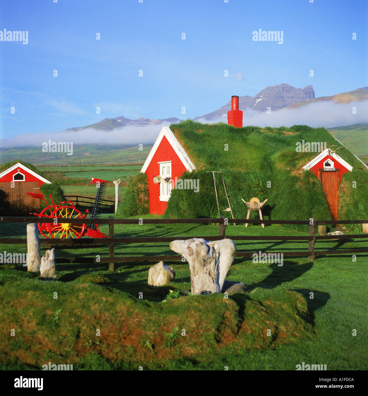 Turf houses covered in grass with farm implements outside and low cloud ...