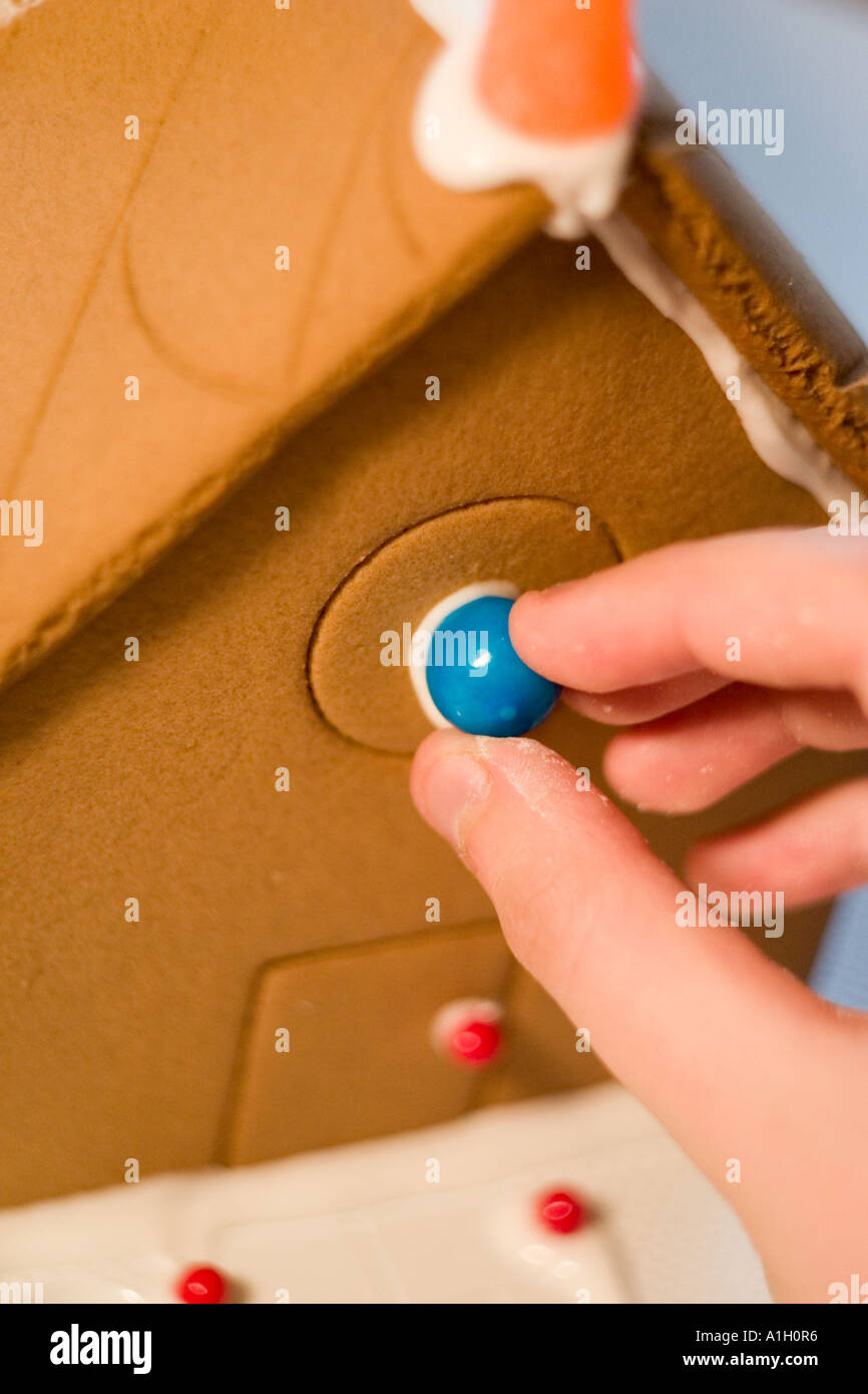 Gingerbread house making fingers holding blue round candy in frosting ...