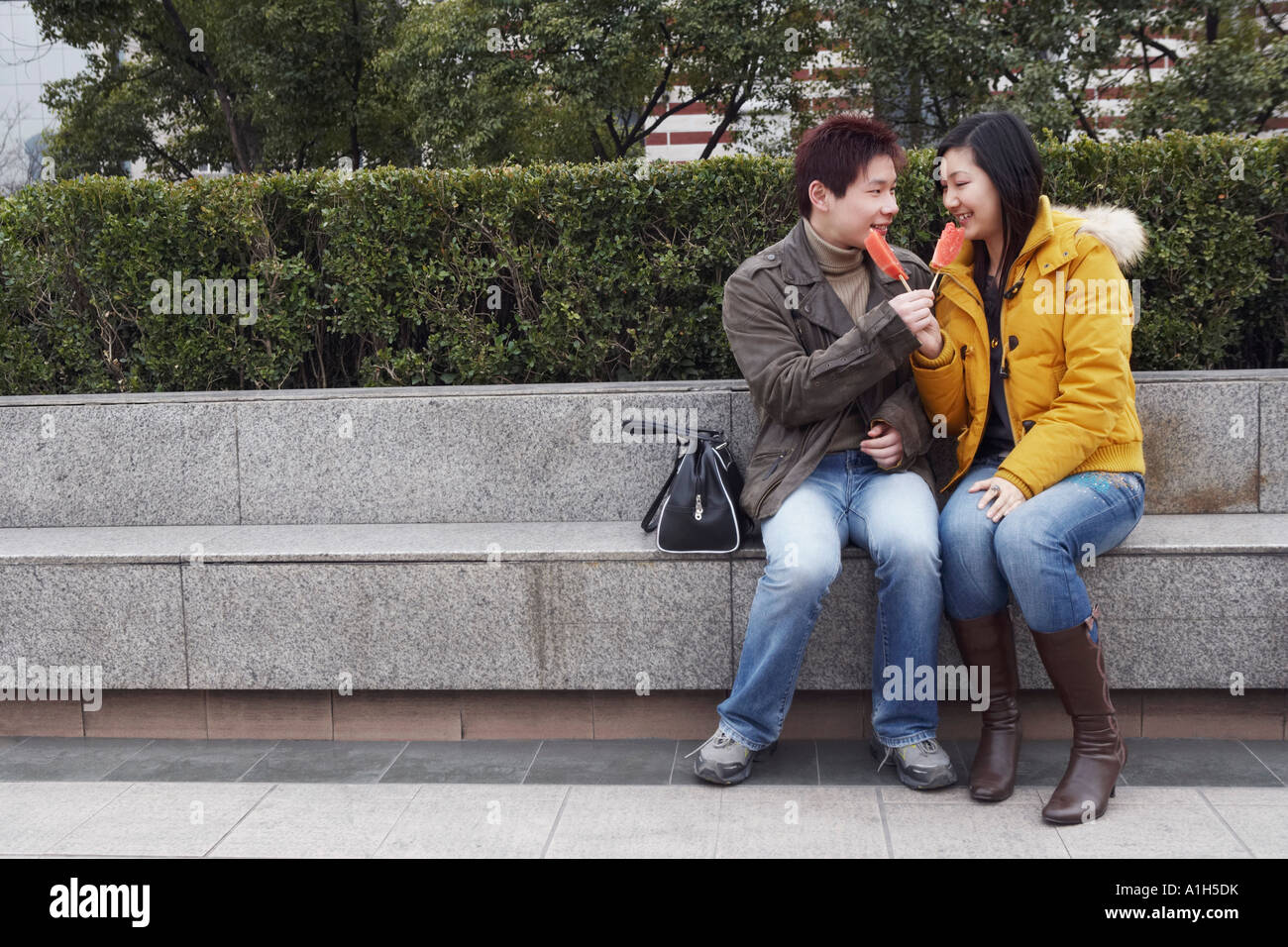 Young man and a young woman sitting on a ledge eating watermelon Stock ...