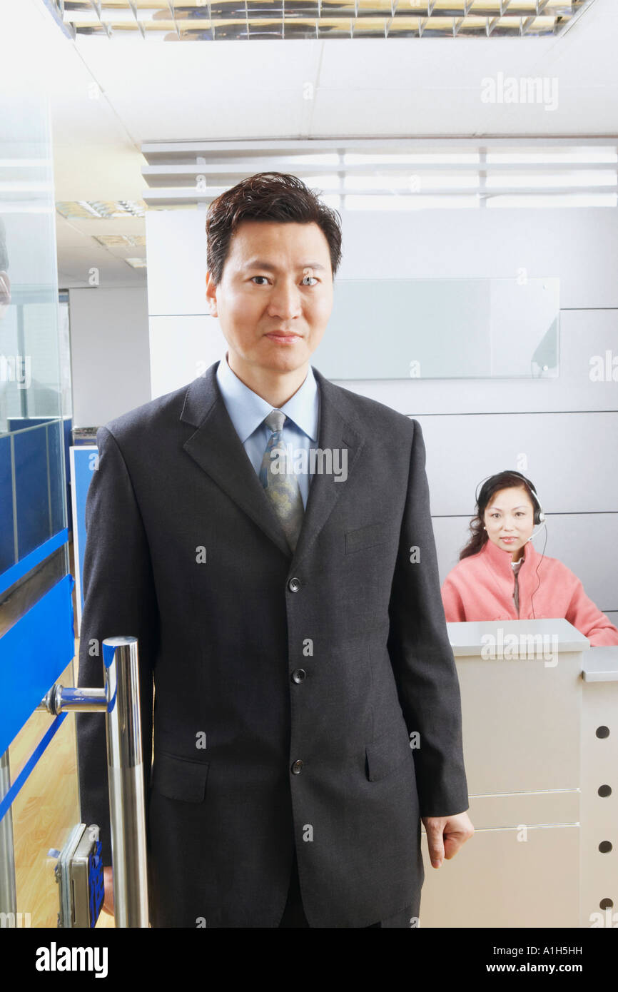 Portrait of a businessman standing in office with a receptionist behind ...