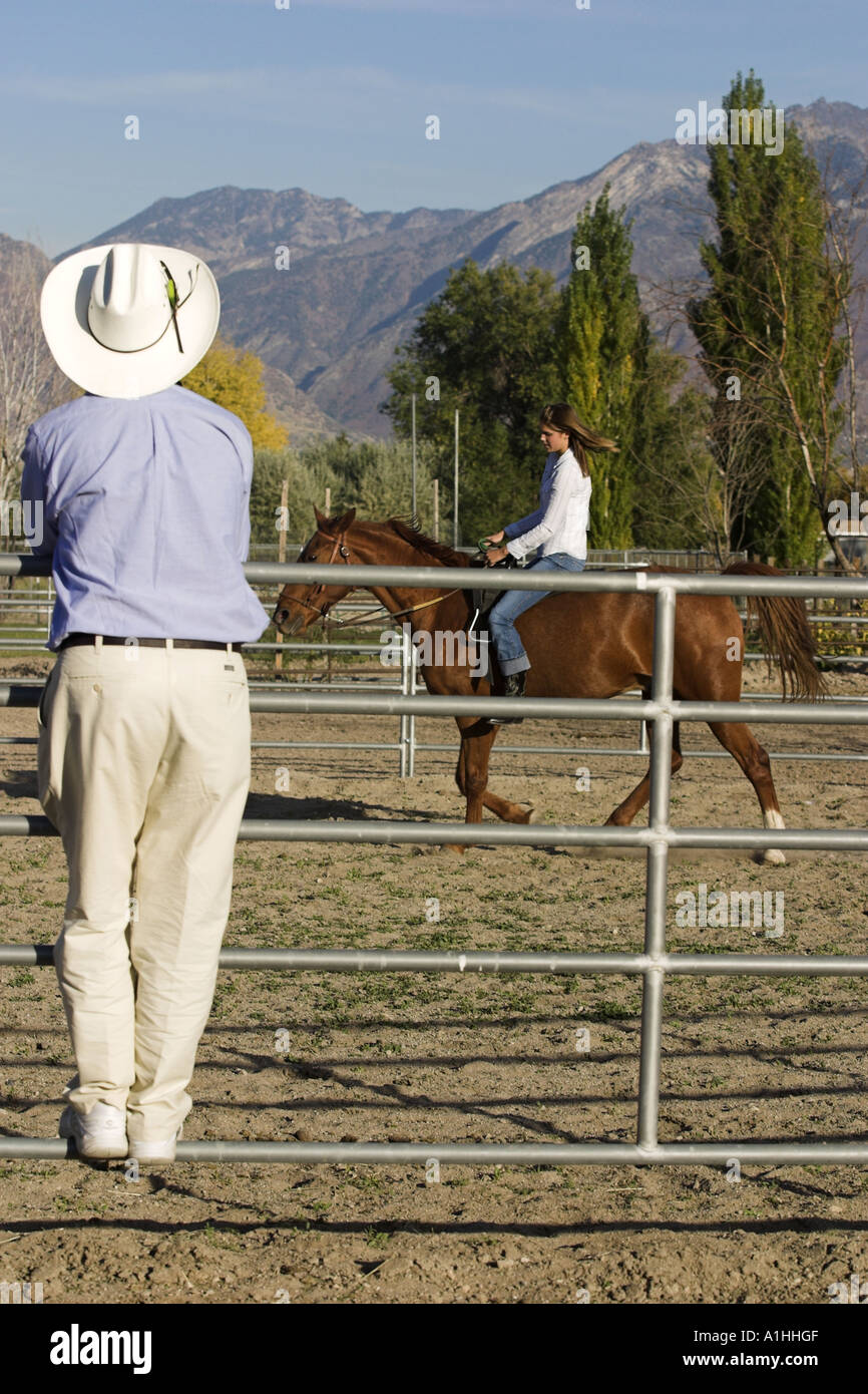 Back view of a man wearing a cowboy hat standing on corral fence ...
