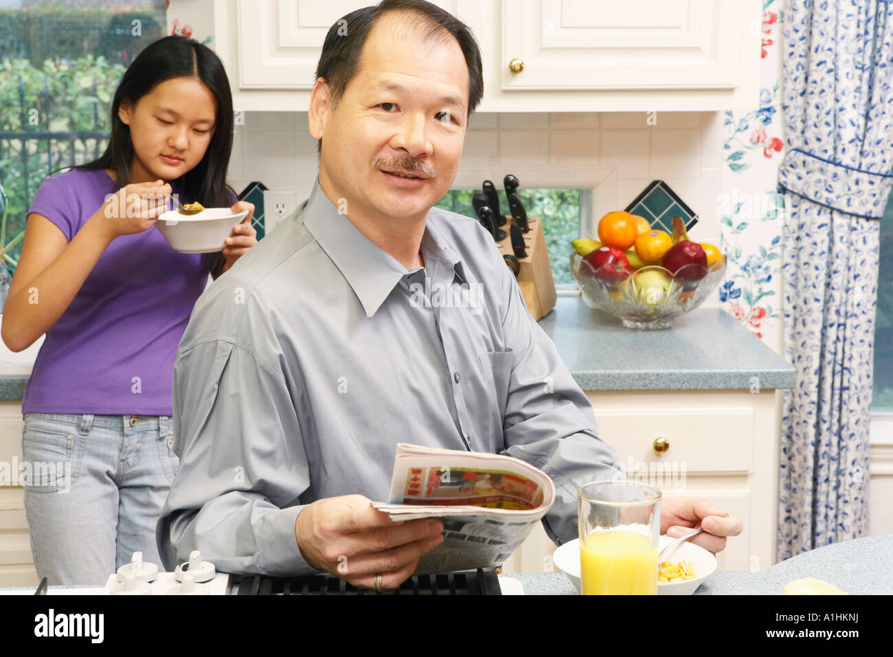 Portrait of a father holding a newspaper with his daughter eating ...