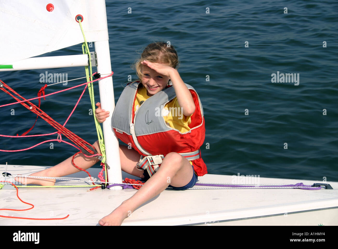 Young girl happily sitting on the foredeck of a laser sailing dinghy ...