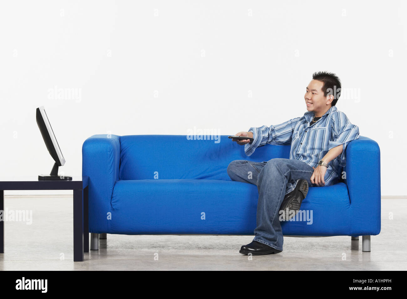 Side profile of a young man holding a remote control sitting in front ...