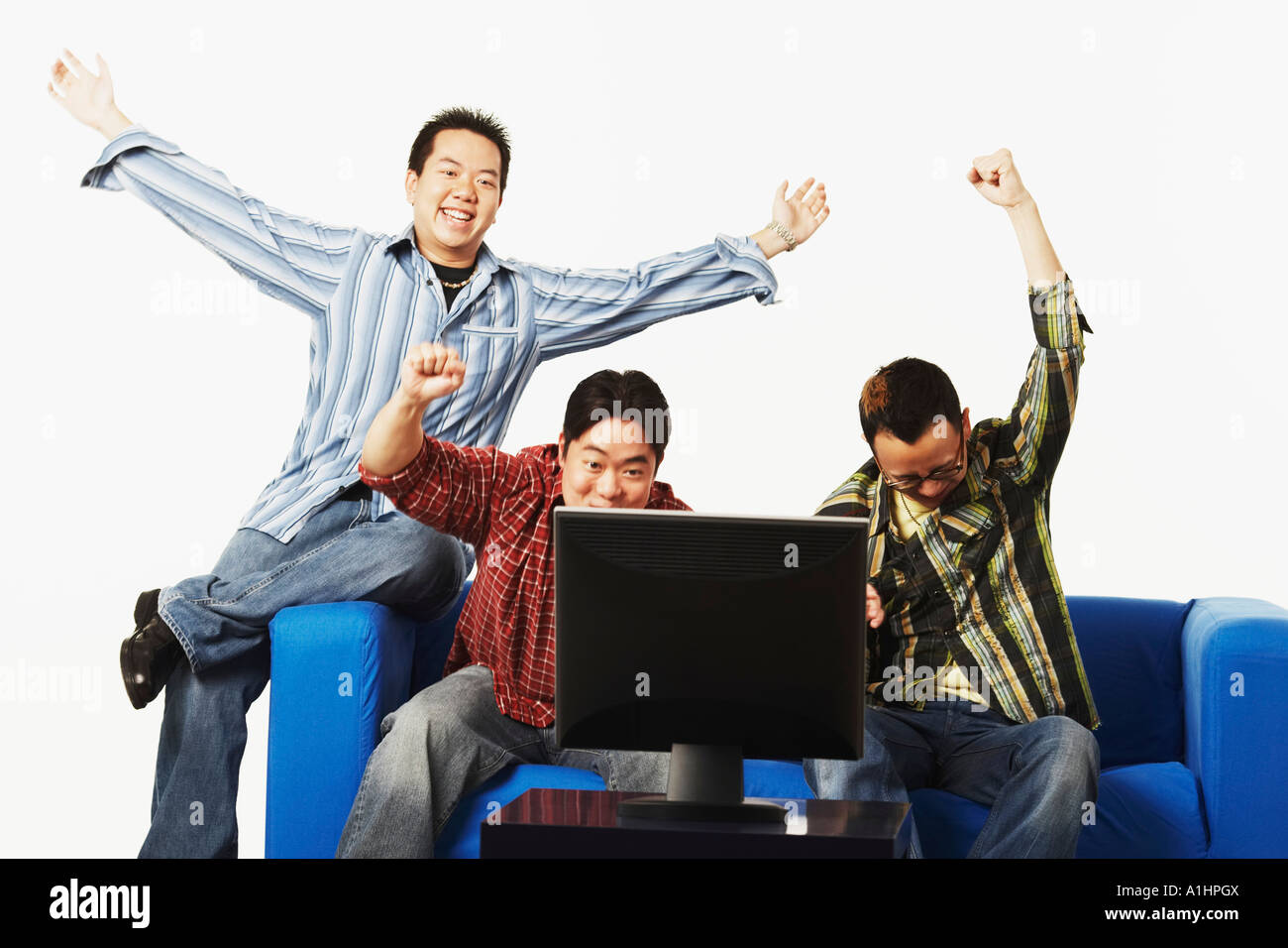 Three young men sitting on a couch in front of a flat screen monitor ...