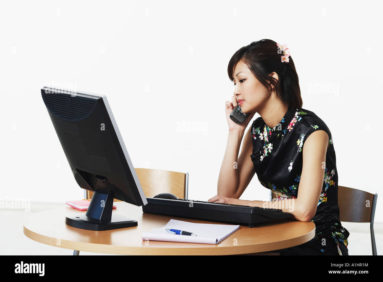Young woman sitting in front of a computer talking on the telephone ...