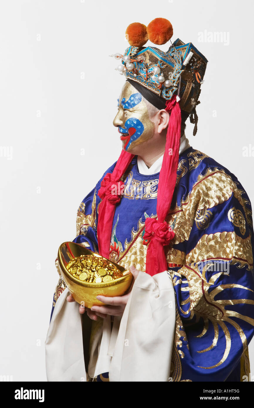 Close-up of a male Chinese opera performer holding a bowl full of gold ...