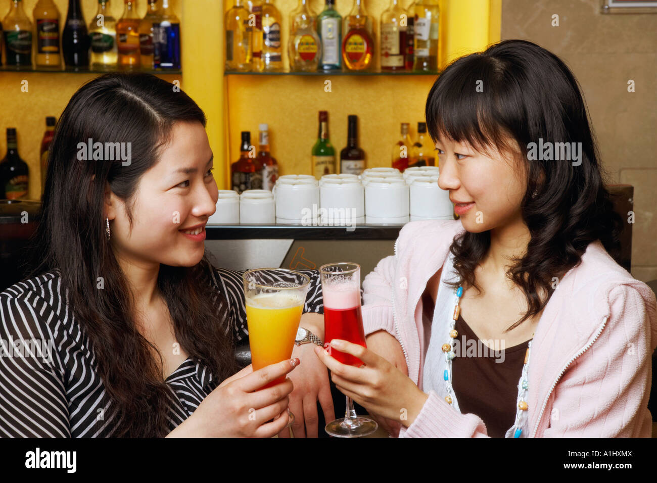 Two young women sitting at a bar counter raising a toast Stock Photo ...