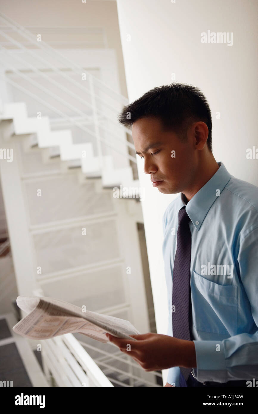 Side profile of a businessman leaning against a wall and reading a ...