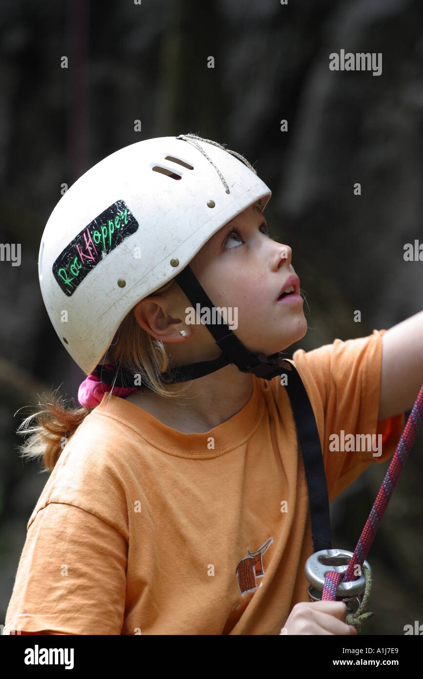Young girl rock climbing rock face with helmet and safety rope in the ...