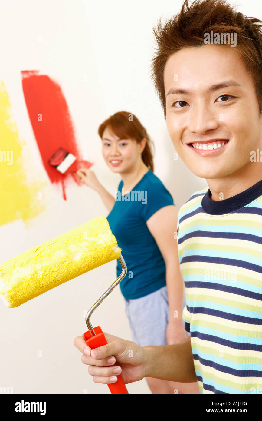 Portrait of a young man holding a paint roller with a young woman ...
