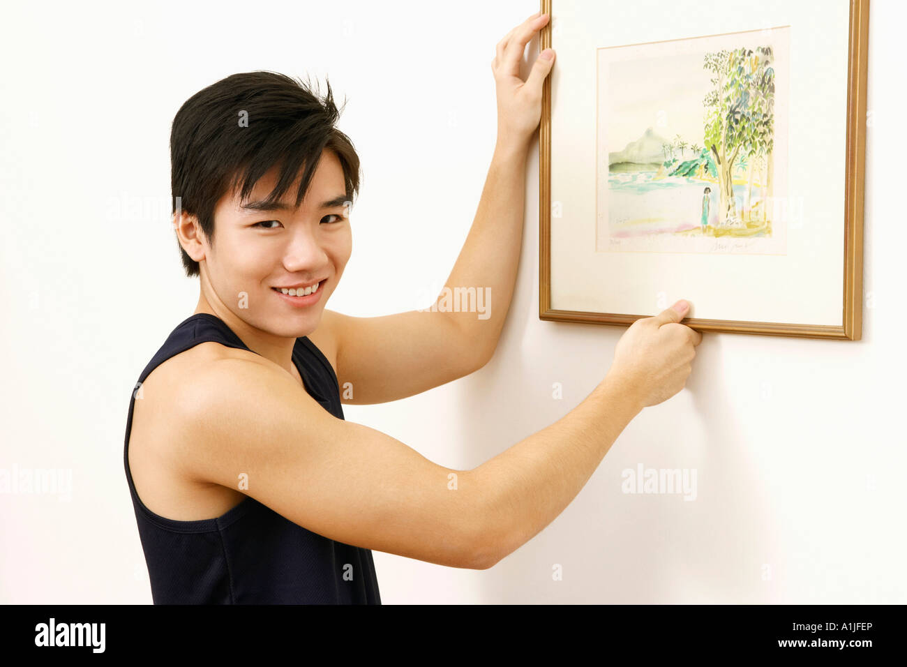 Portrait of a young man hanging a picture frame on wall and smiling ...