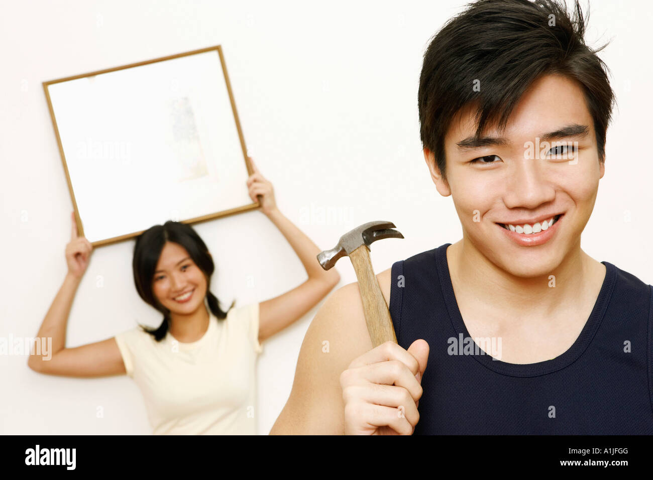 Portrait of a young man holding a hammer with a young woman standing in ...
