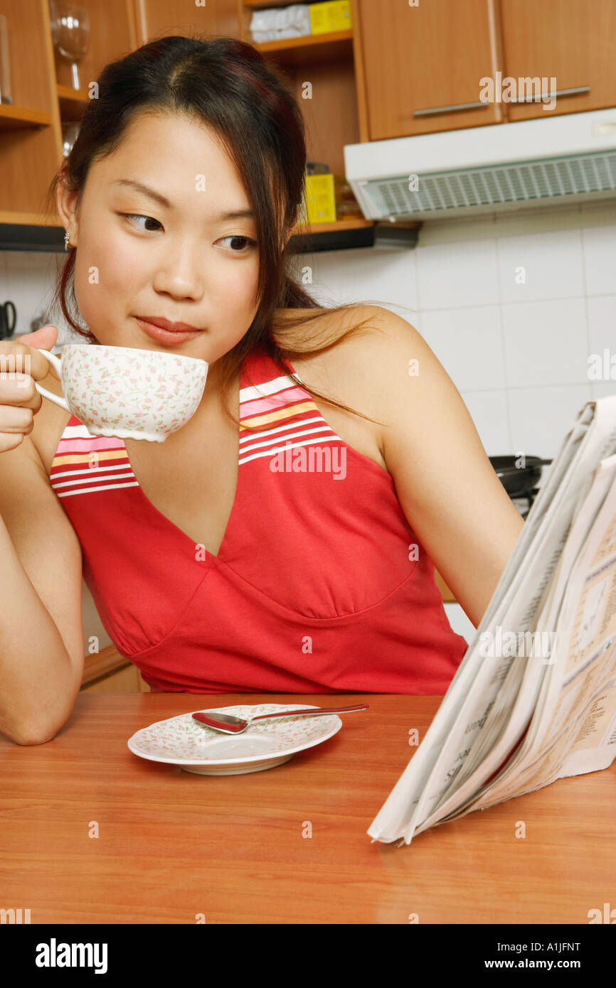 Close-up of a young woman reading a newspaper at a kitchen counter ...