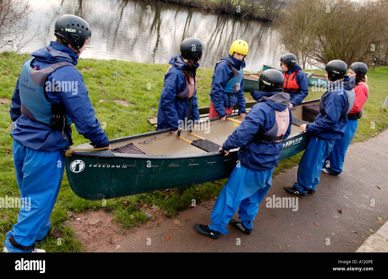 Students showing teamwork while launching an open canoe on the banks of ...