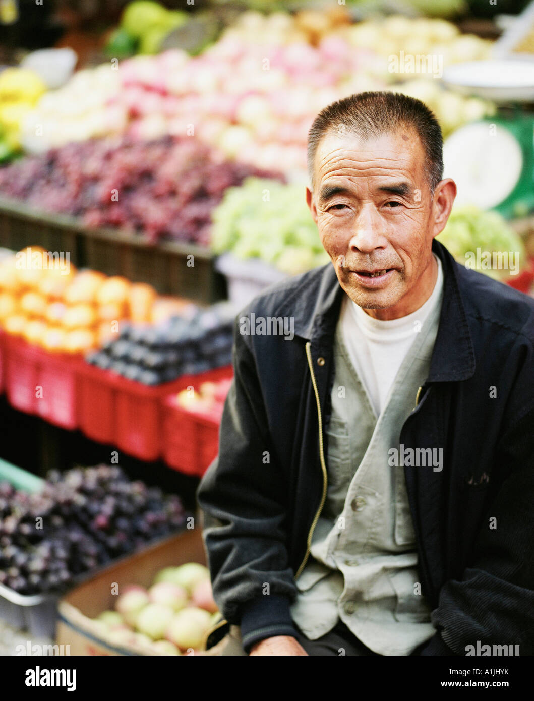High angle view of a senior man sitting in front of a vegetable stand ...