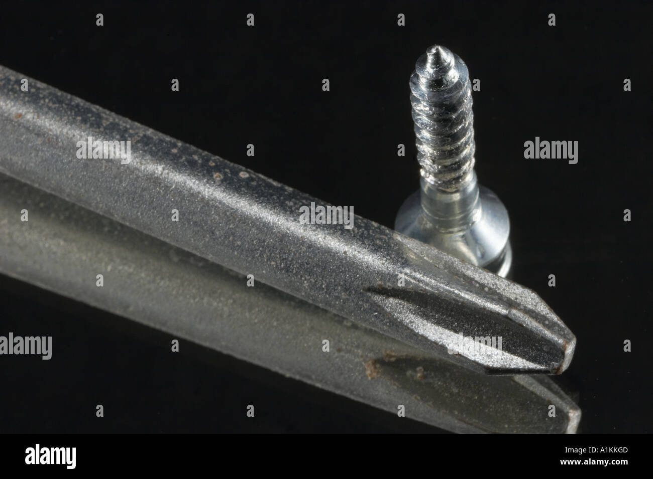 A screwdriver and a screw on a black background with a mirror ...