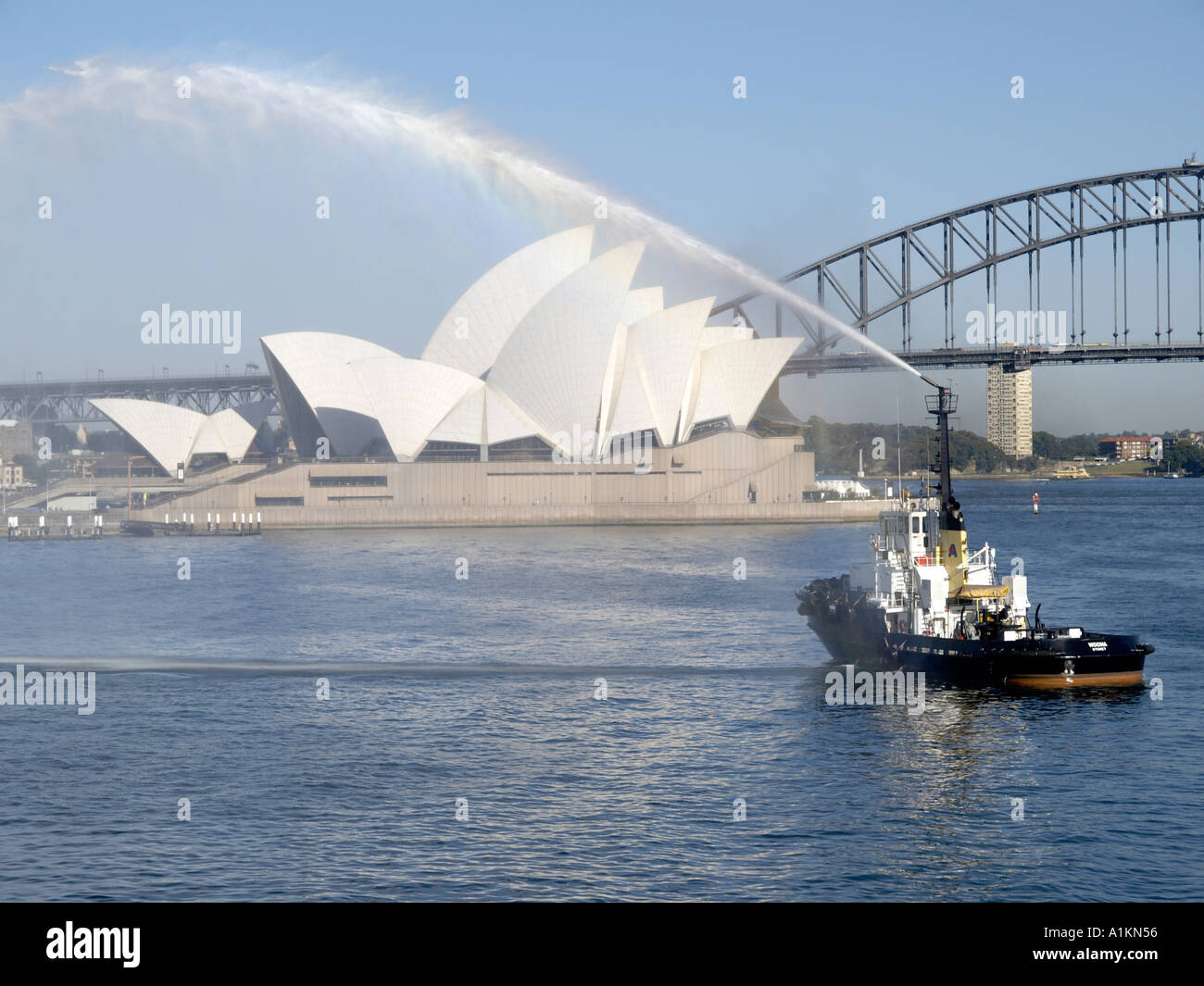TUG BOAT WITH JET OF WATER BEING FIRED INTO AIR WITH OPERA HOUSE IN THE ...