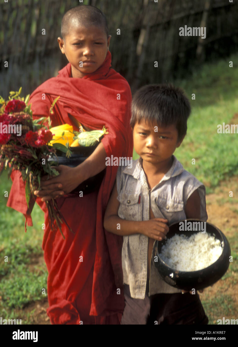Boy monk and his small brother with rice and flowers from an alms round ...