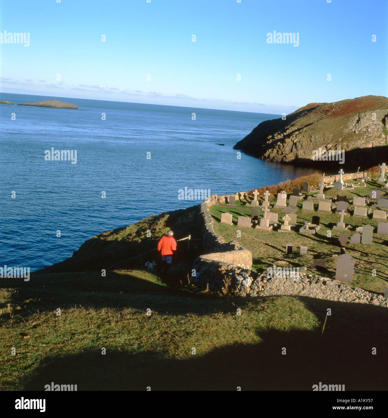 A man walking the coastal path by the seaside cemetery at Llanbadrig ...