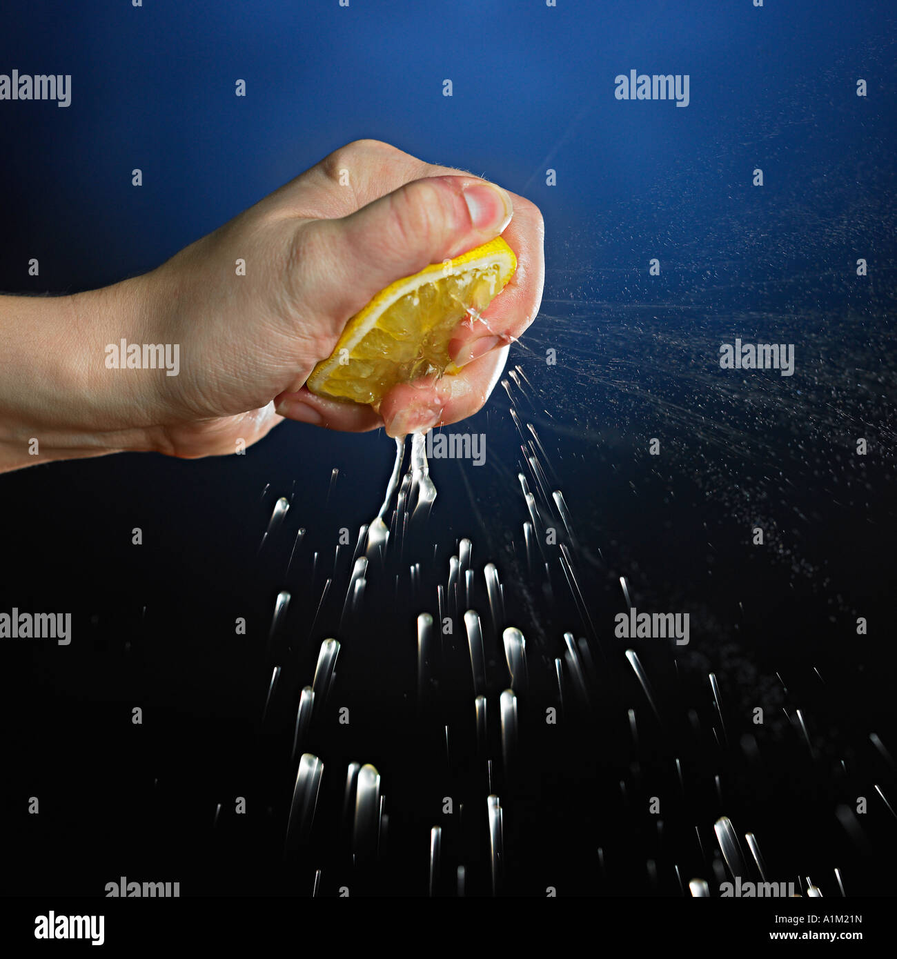 A hand squeezing a lemon in front of a blue backdrop Stock Photo - Alamy