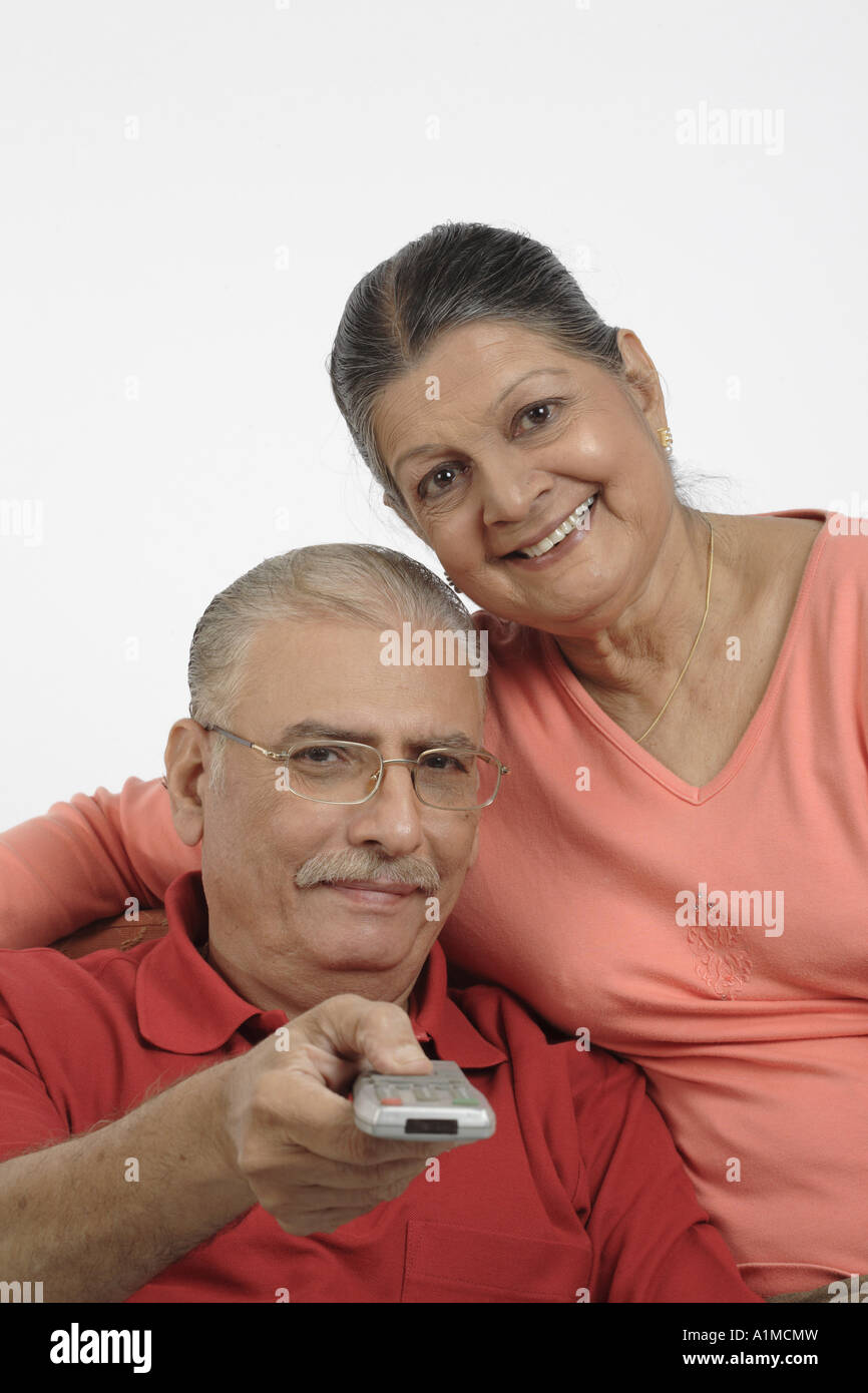 Happy Indian senior citizen couple pressing remote on white background ...