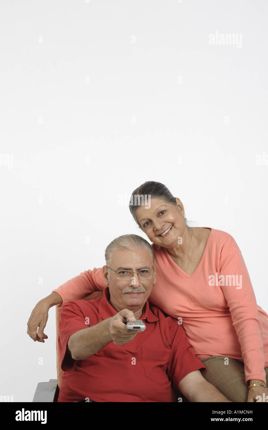 Happy Indian senior citizen couple pressing remote on white background ...