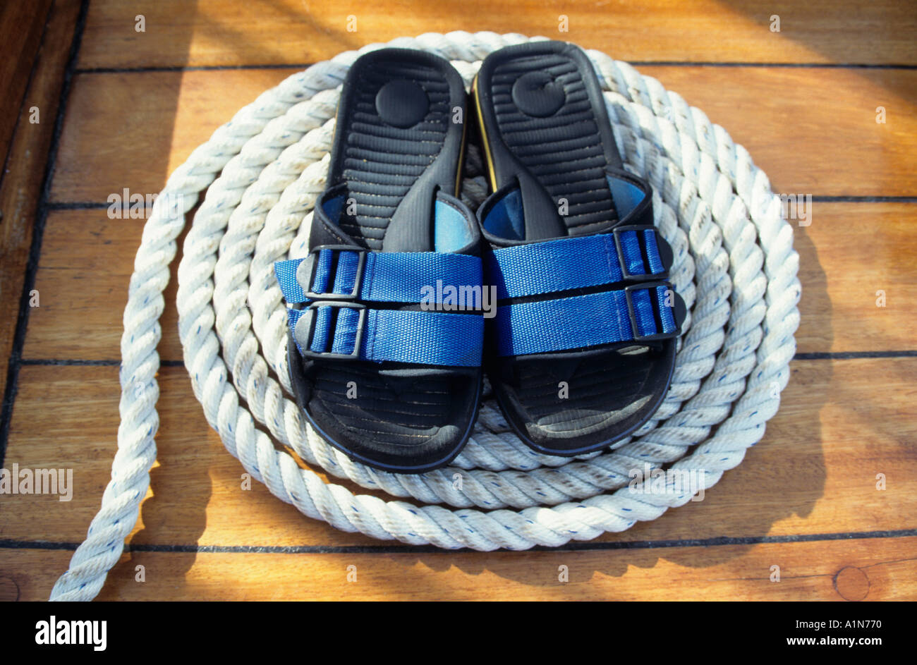 Pair of blue flip flops neatly centred on a coiled rope on the teak ...