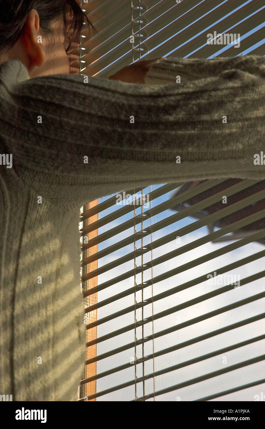 Young woman standing looking through window blinds Stock Photo - Alamy