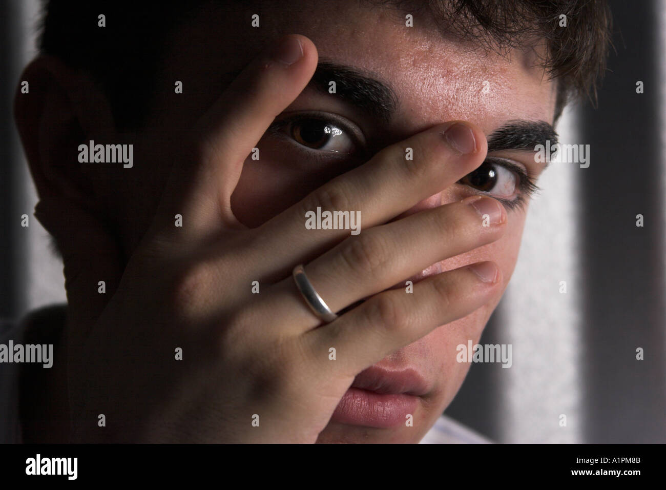 Young man hiding his face behind his hand Stock Photo - Alamy