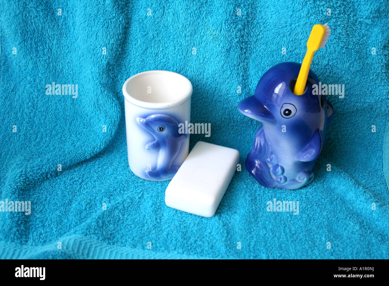Dolphin-themed toothbrush holder and cup on a blue towel with a bar of ...
