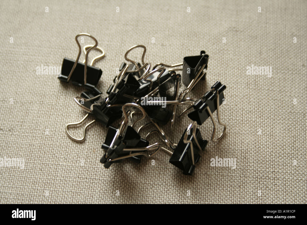 : A pile of black binder clips on a textured fabric surface, commonly ...