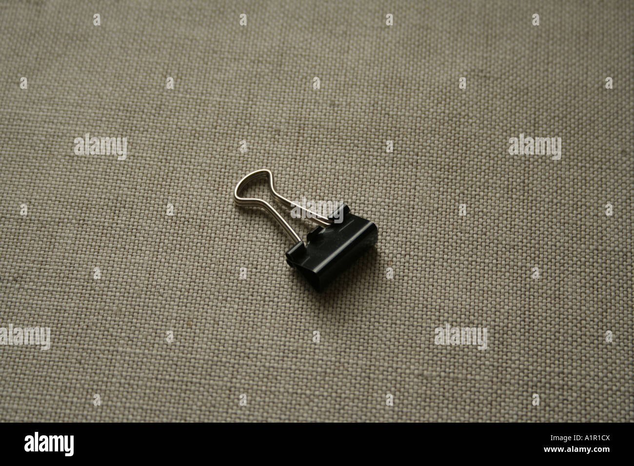 Single black binder clip on a textured fabric surface, commonly used ...