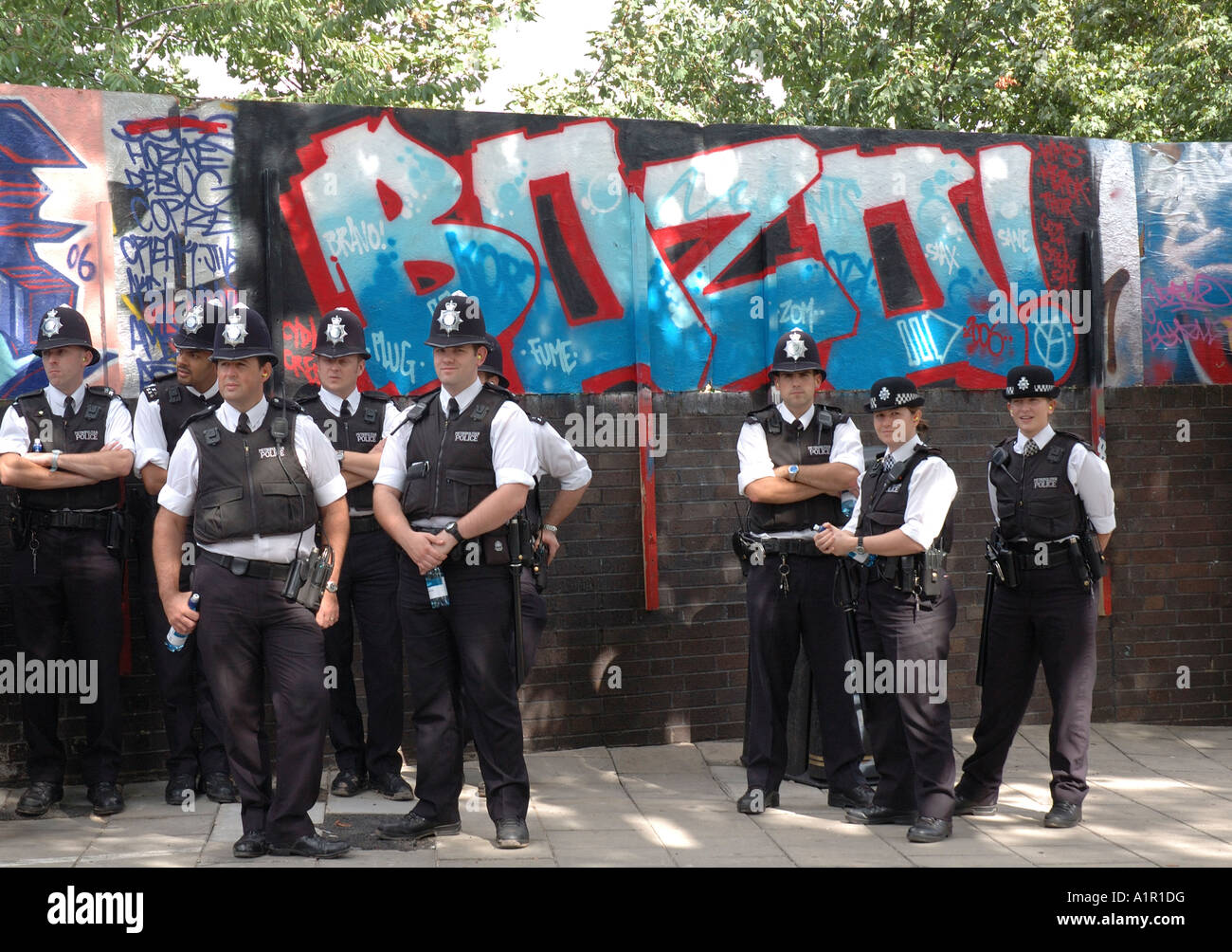Line-up of police in front of inner city London graffiti wall Stock ...