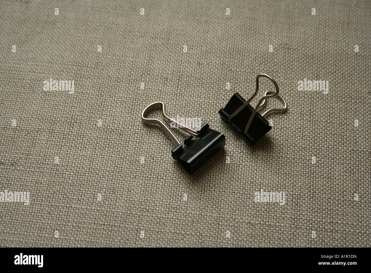 Two black binder clips on a textured fabric surface, useful for ...
