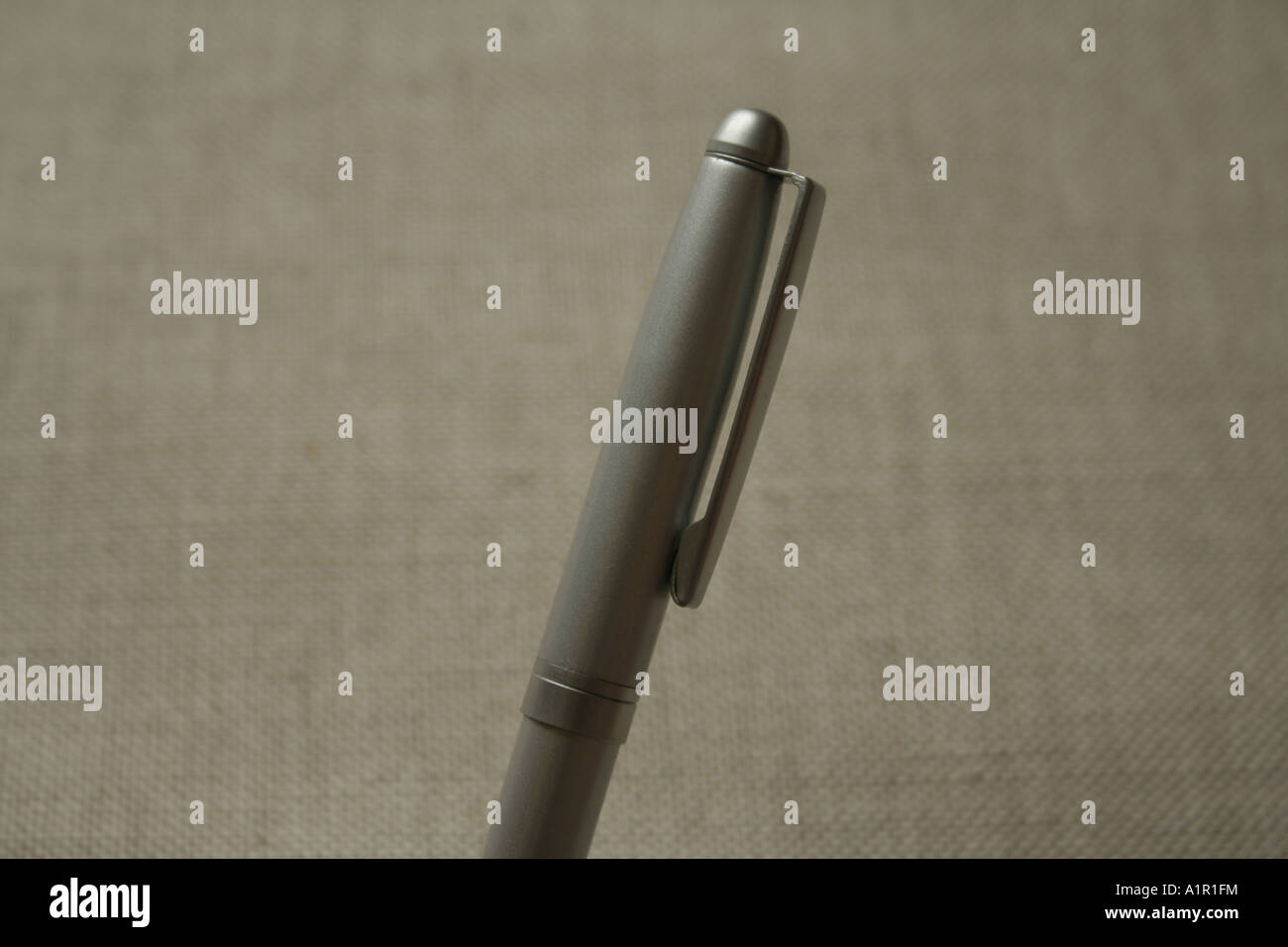 A close-up of a silver pen standing upright on a textured fabric ...