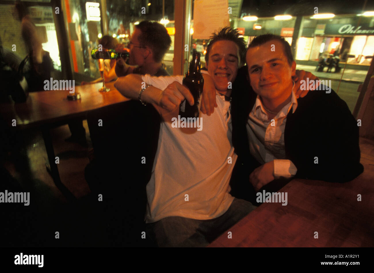 Two young men with their arms round each others necks drink beer in one ...