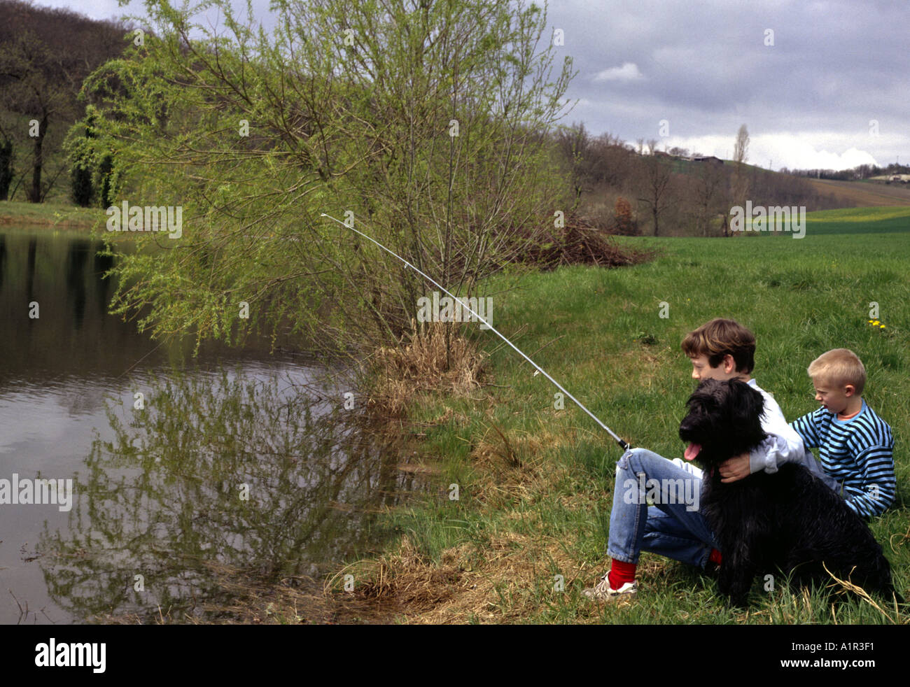 two boys with a dog angling at a river MR Stock Photo - Alamy