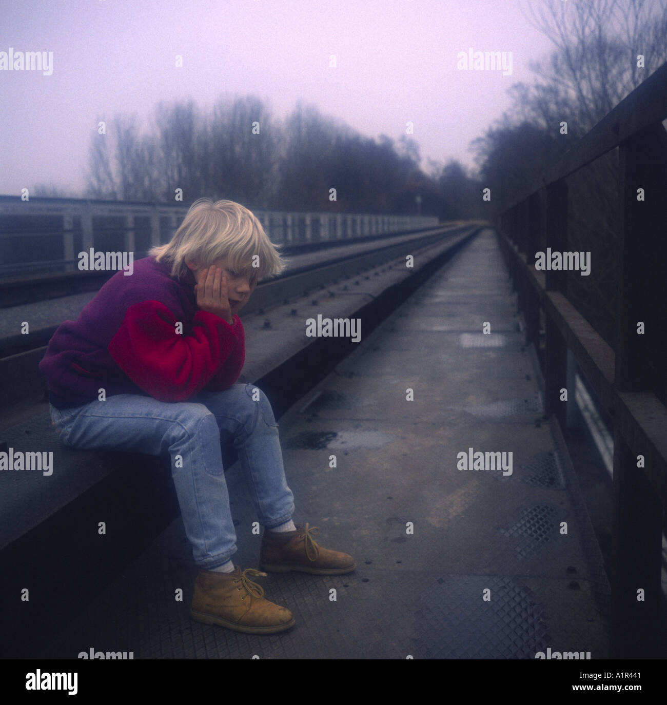 fair haired boy sitting sad and bored in fog on an empty bridge MR ...
