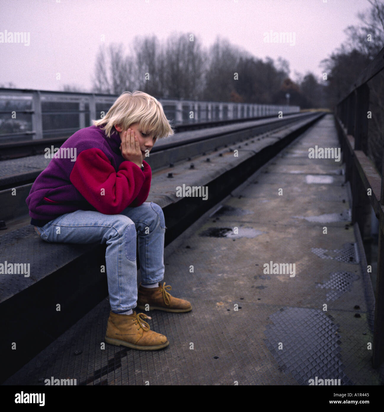 fair haired boy sitting sad and bored on an empty bridge MR Stock Photo ...