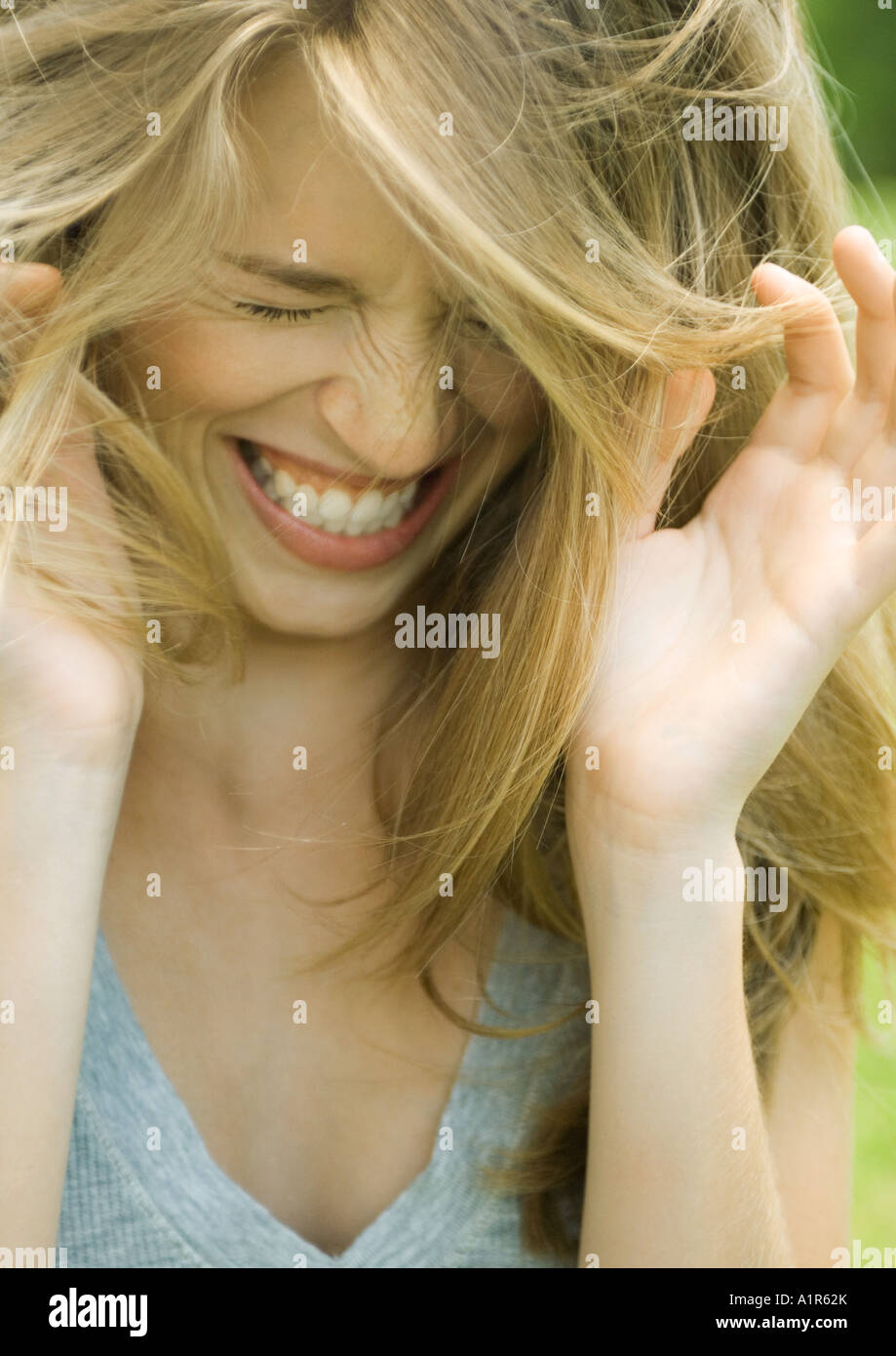 Young woman lowering head, shutting eyes and laughing with hands up ...