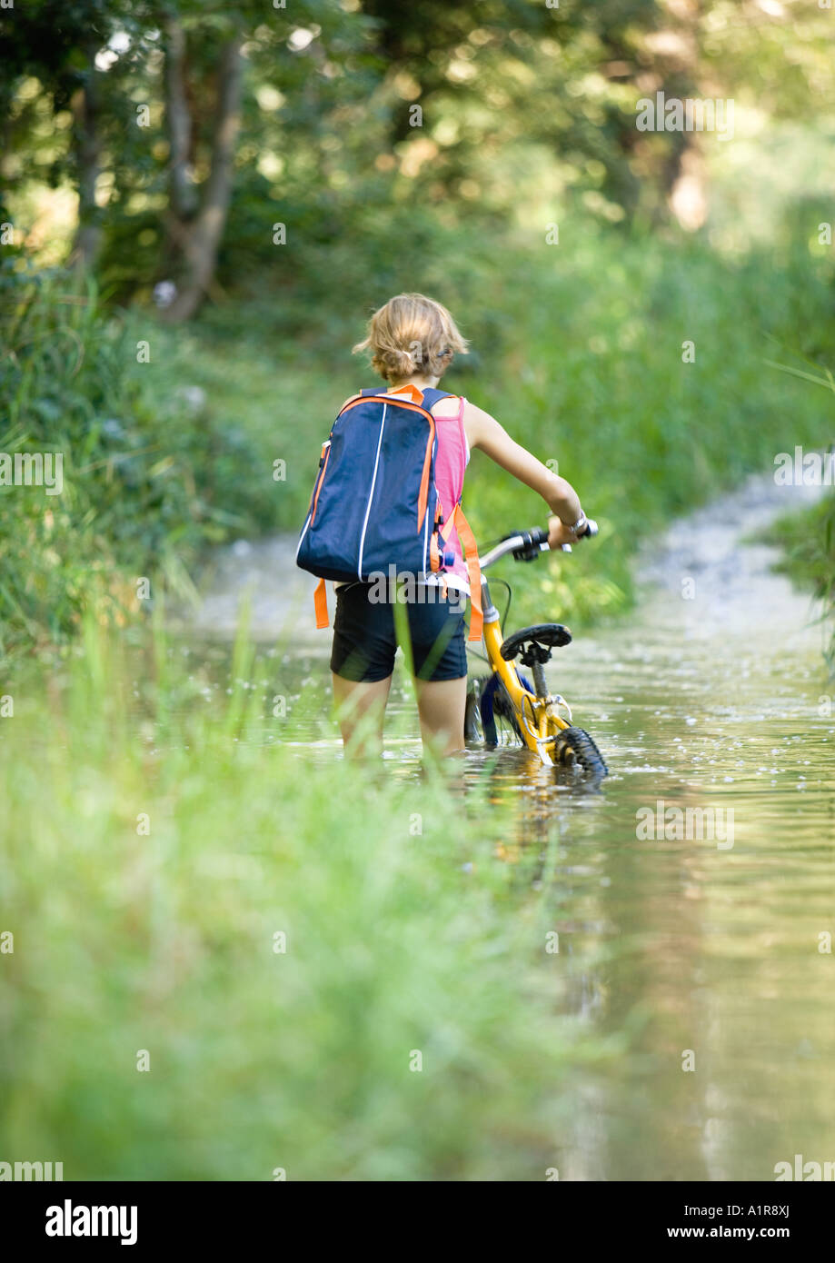 Girl walking through water with bike, rear view Stock Photo - Alamy