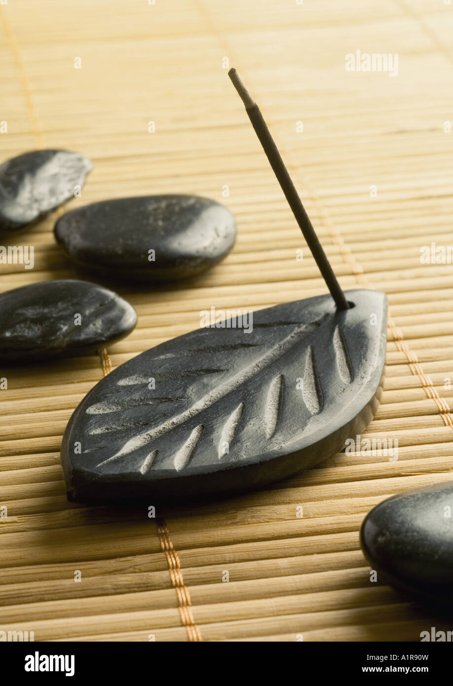 Stick of incense burning in incense holder and smooth black stones ...