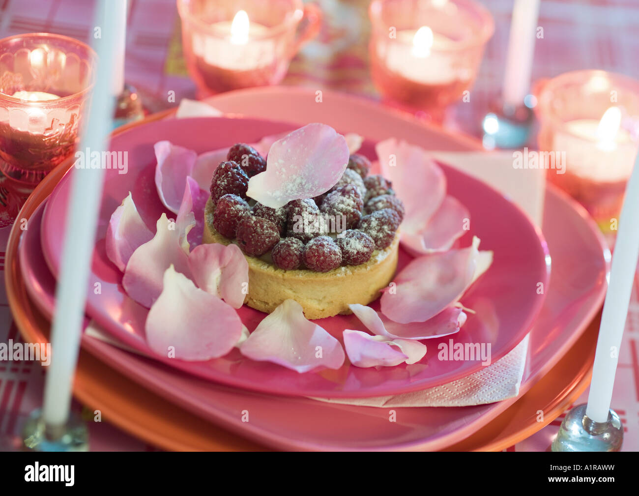 Raspberry tartlet on plate decorated with rose petals, surrounded with ...