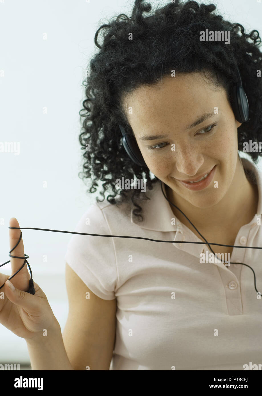 Woman listening to headphones, wrapping cord around finger Stock Photo ...