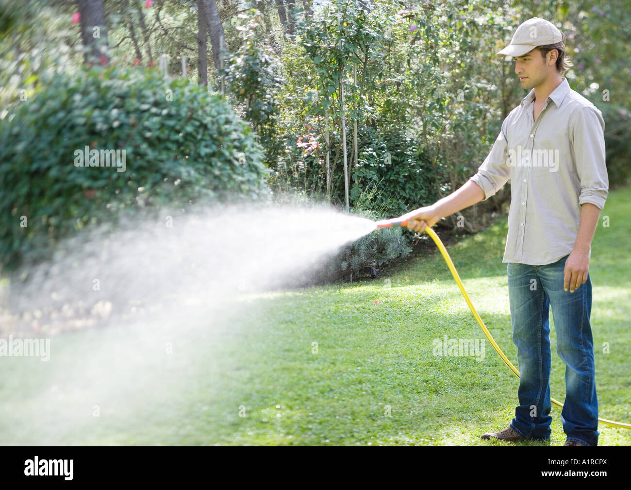 Man doing yardwork, using garden hose Stock Photo - Alamy