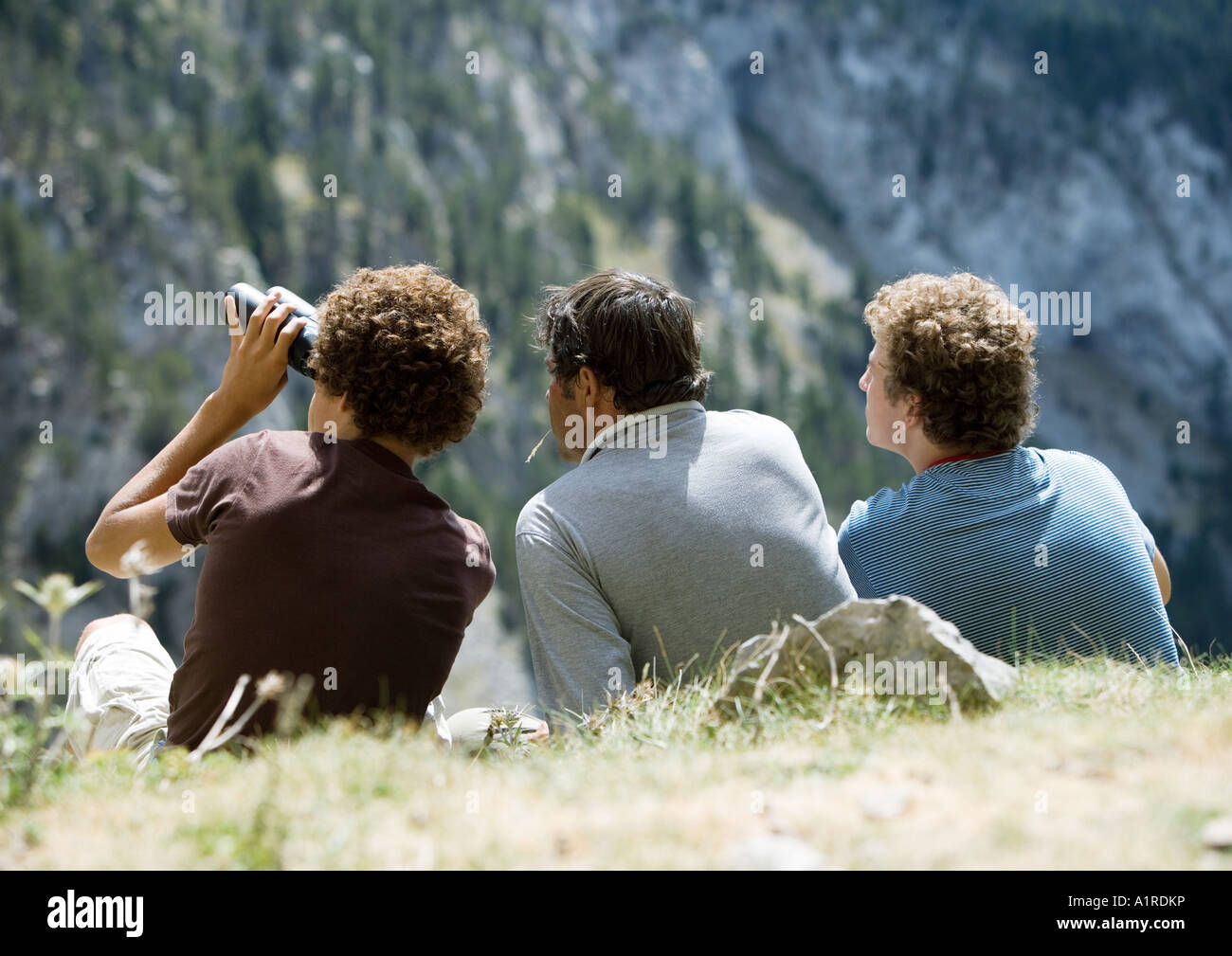 Three men looking at mountain view, one using binoculars Stock Photo ...