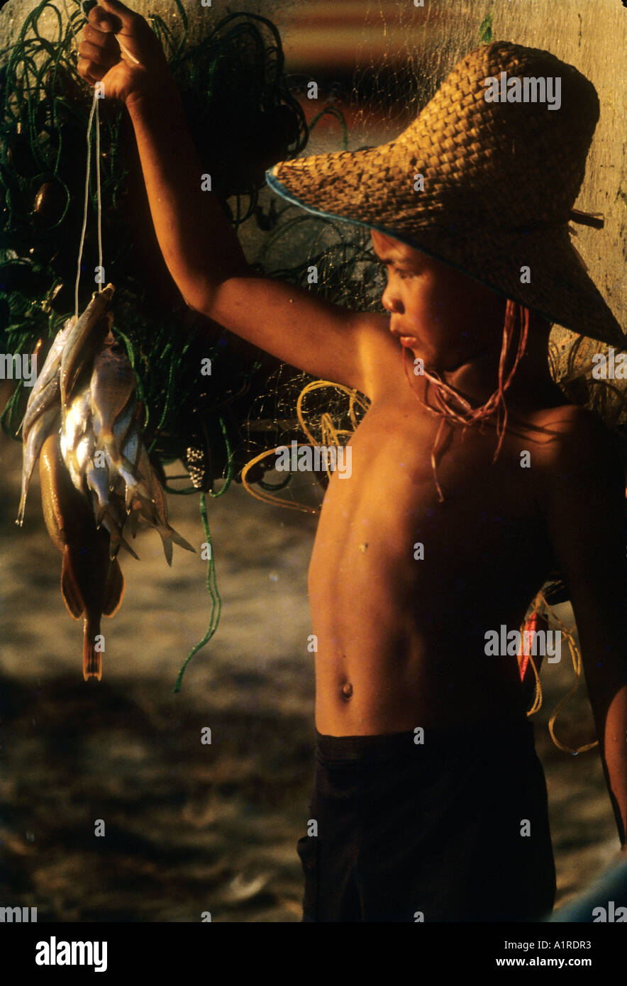 A young fisherboy holds up his meager catch in a very proud stance ...