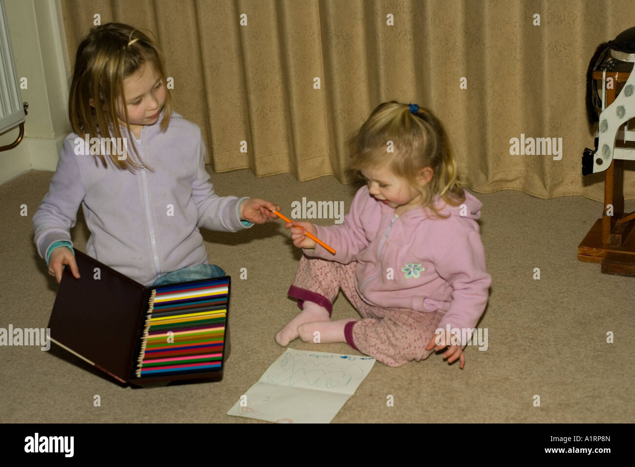 Six year old girl giving pencil to her two year old sister UK Stock ...
